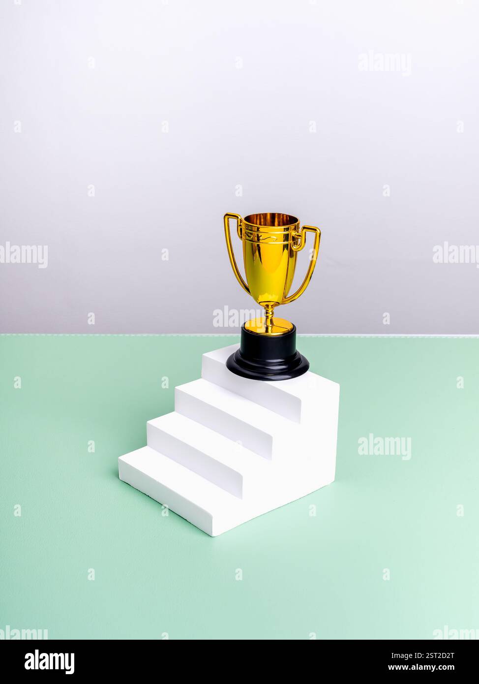 Gold trophy on top of white stair steps as bar graph, on green table ...