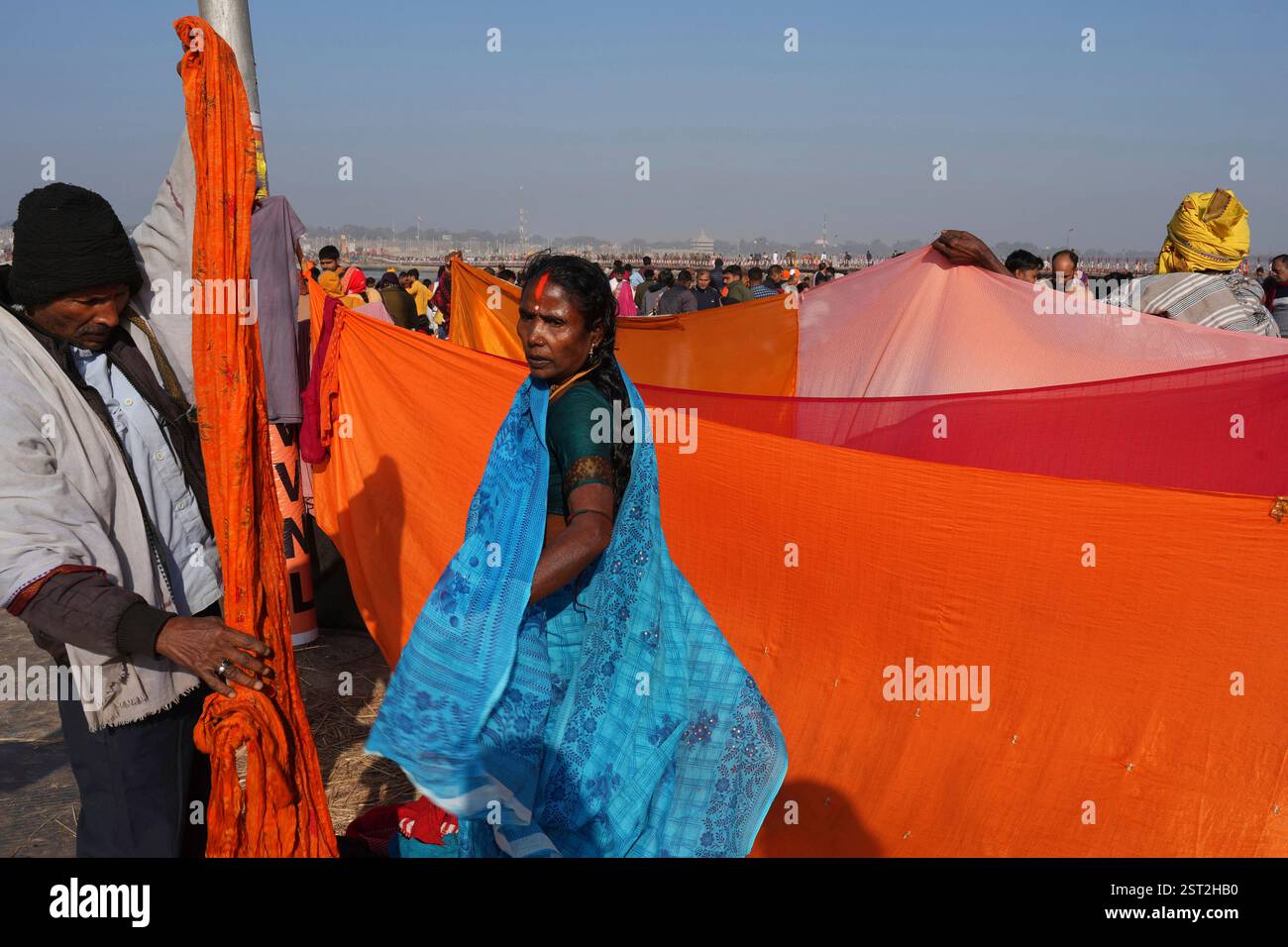 A pilgrim stands next to a sari held up to dry at the confluence of the ...