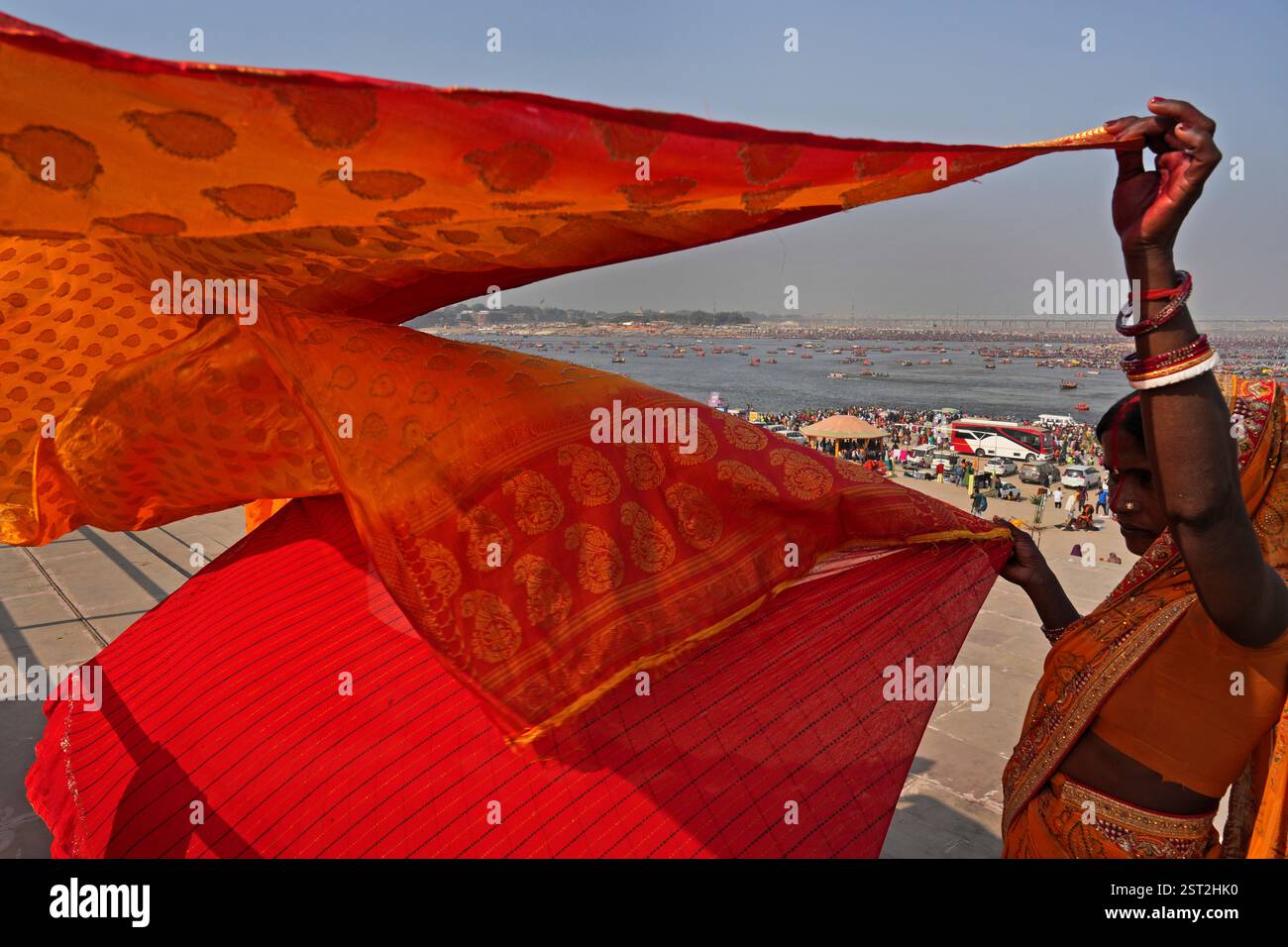 A pilgrim holds up saris to dry after a holy dip at the confluence of ...