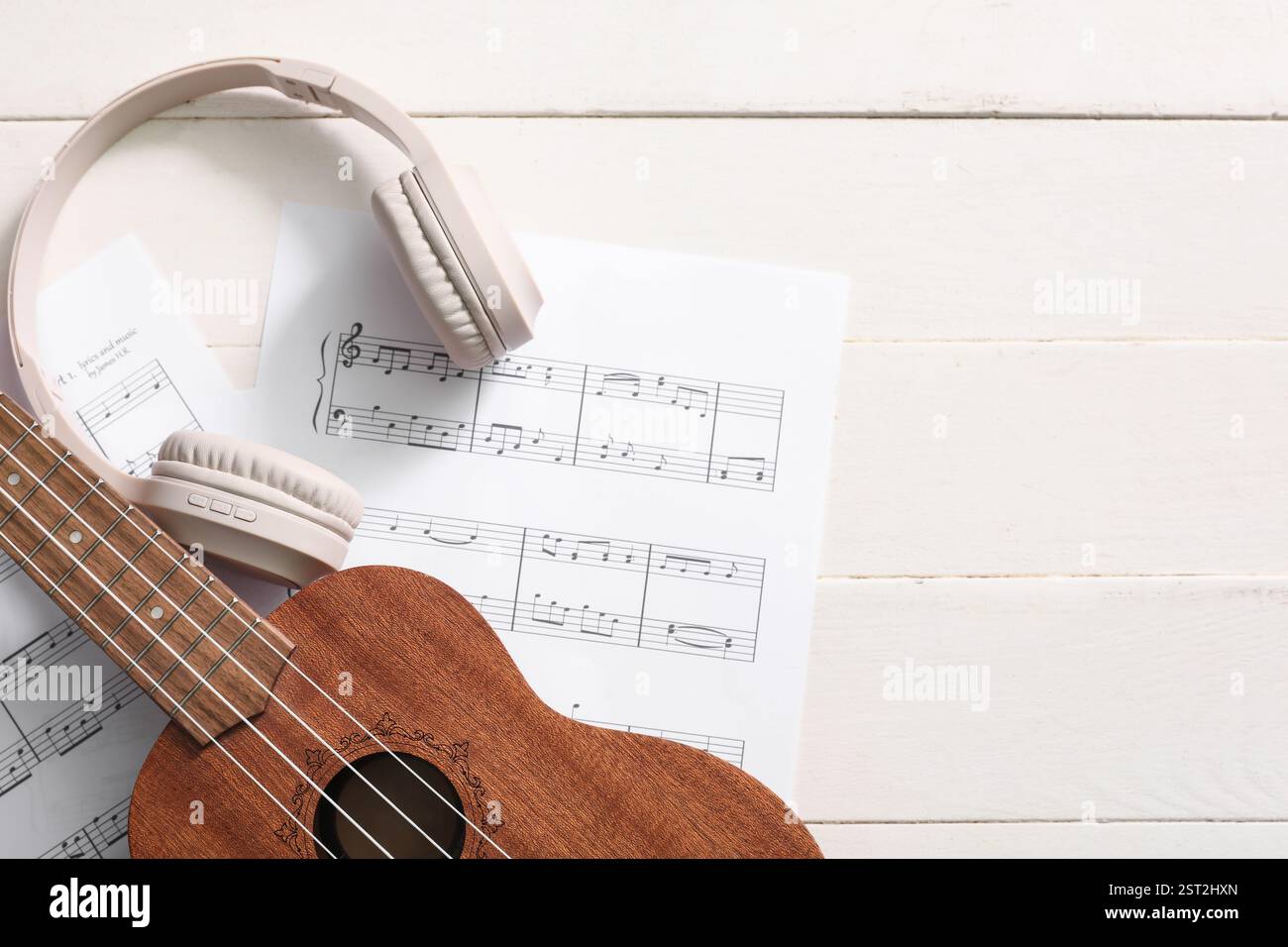 Modern headphones, ukulele and music sheets on light wooden background ...