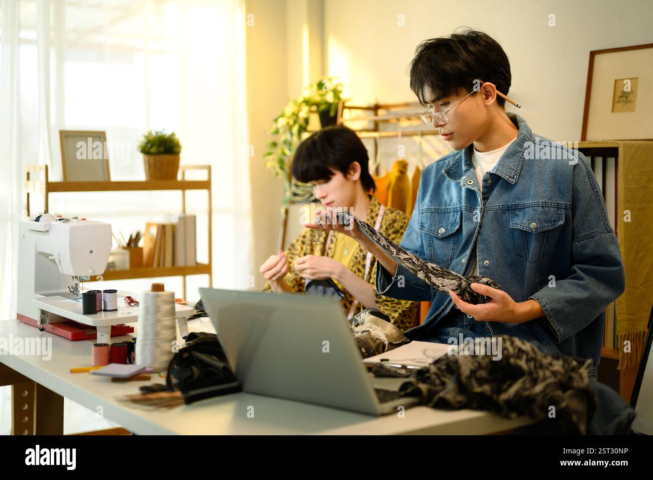 Two fashion designers working together in a studio filled with sewing ...