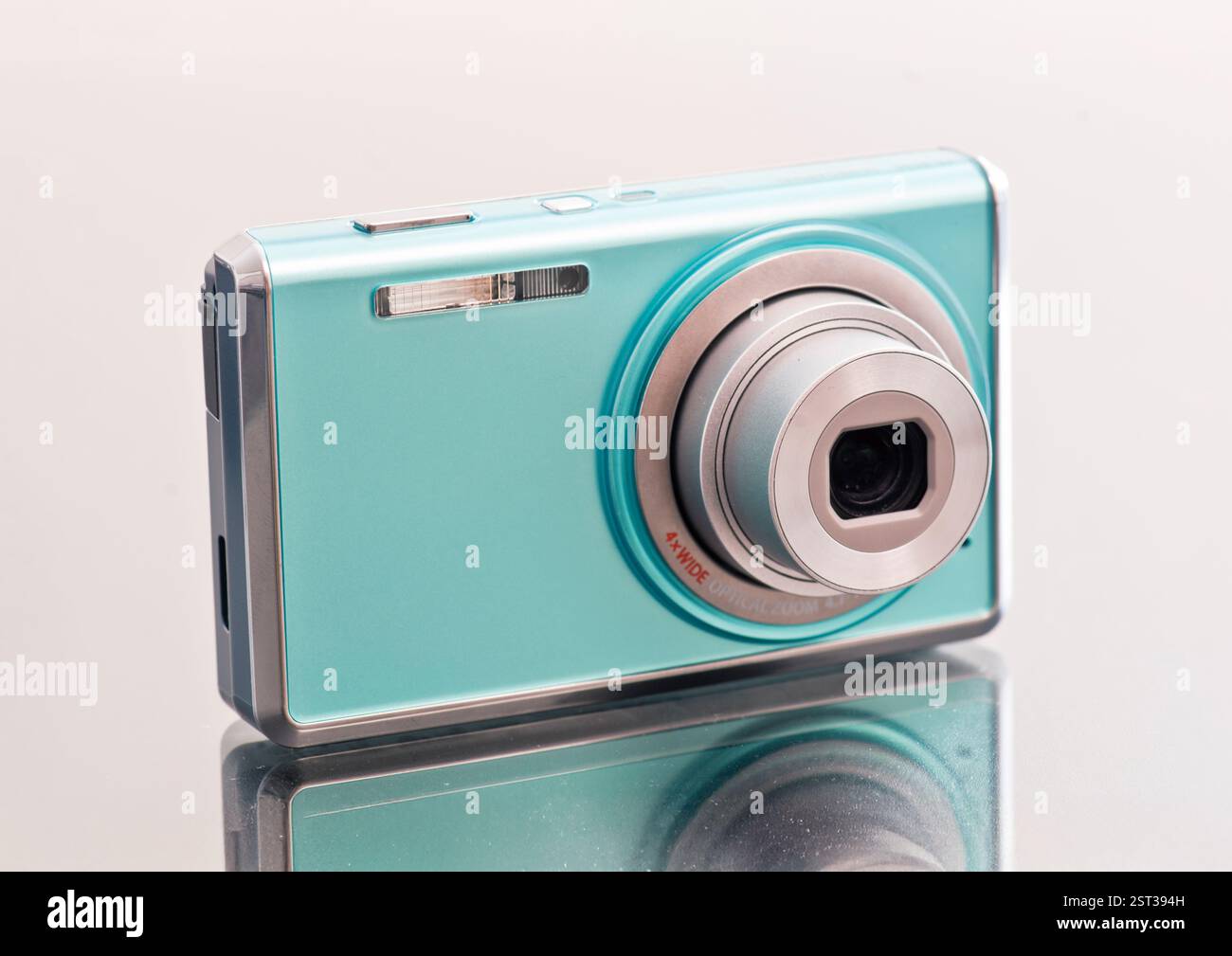 A compact digital camera in a bright blue hue is placed on a shiny ...