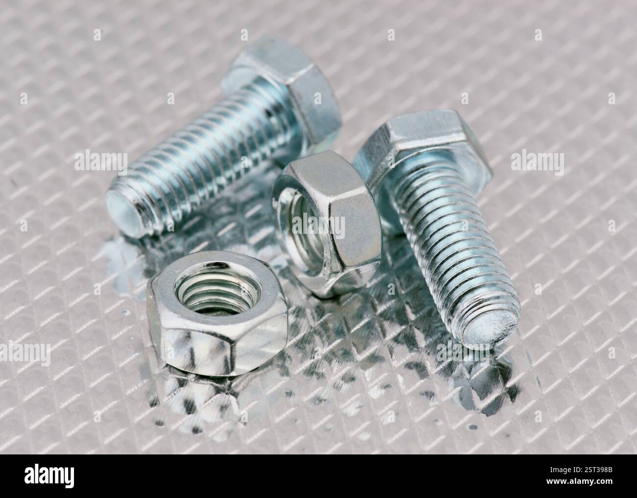 Metal bolts and nuts are arranged on a shiny, reflective surface ...