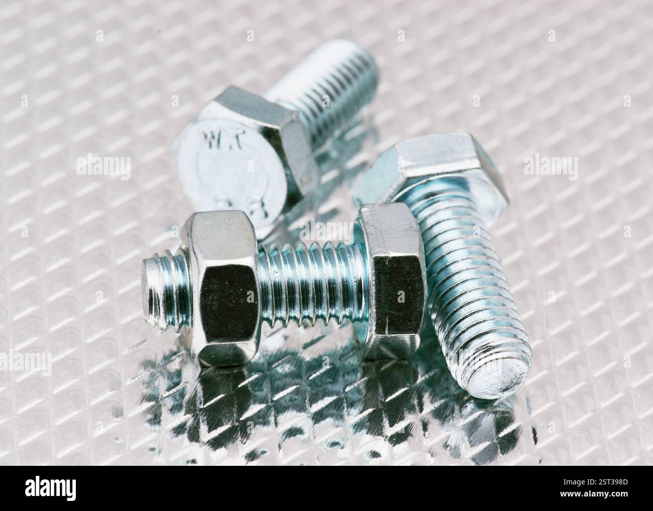 A cluster of metallic bolts and nuts rests on a shiny, reflective ...