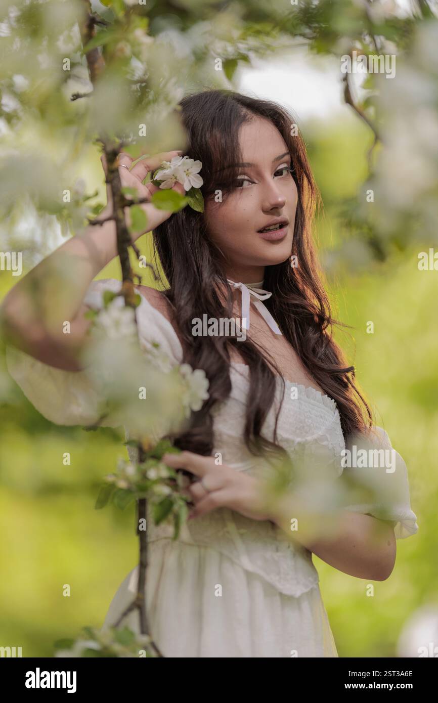 Beautiful Girl with long hair poses near white blossoming apple trees ...