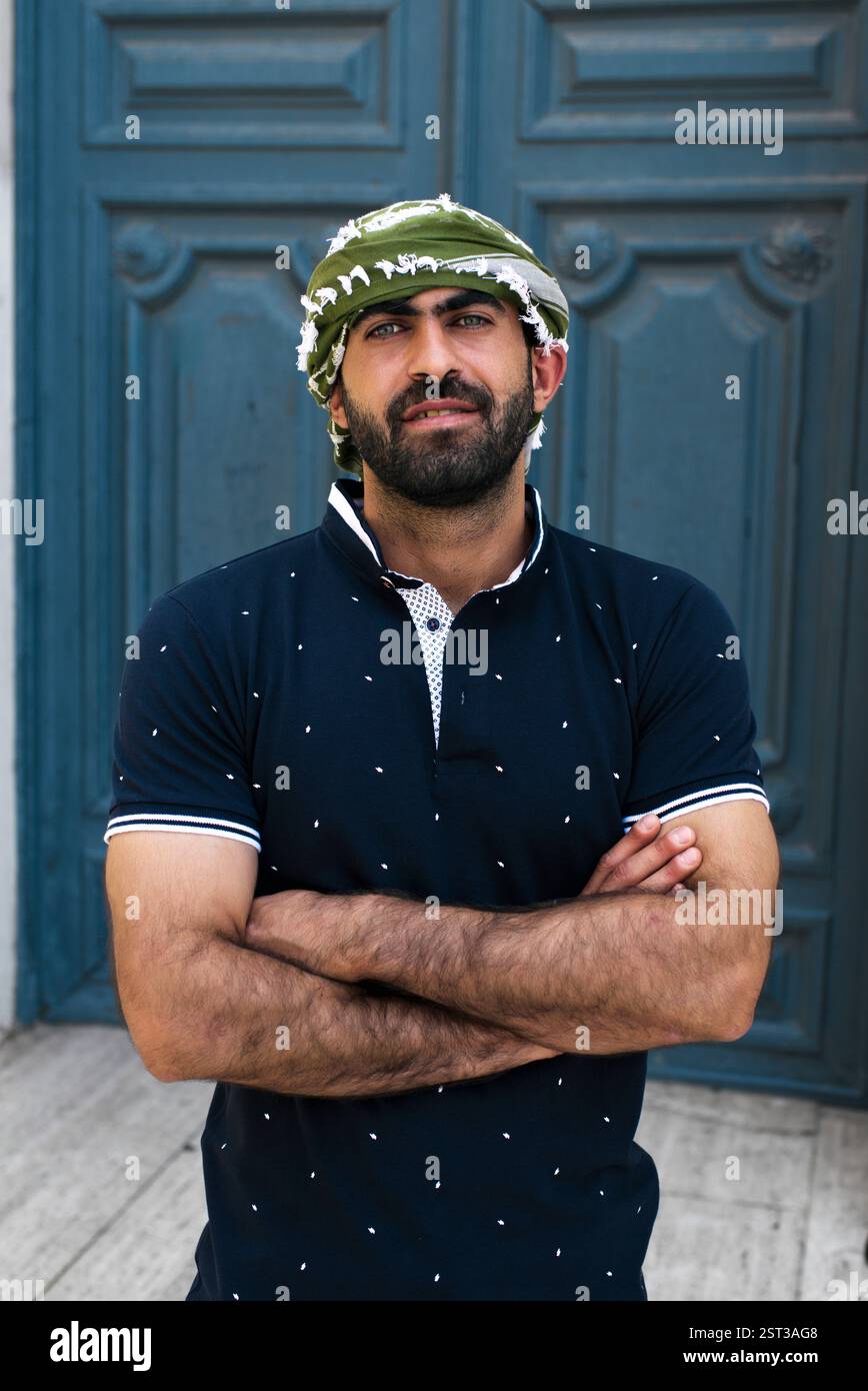 A man with a proud expression stands in front of a blue door, arms ...
