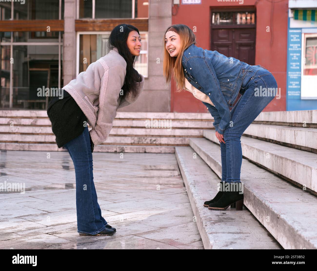 Two friends share a light-hearted moment as they bend forward playfully ...
