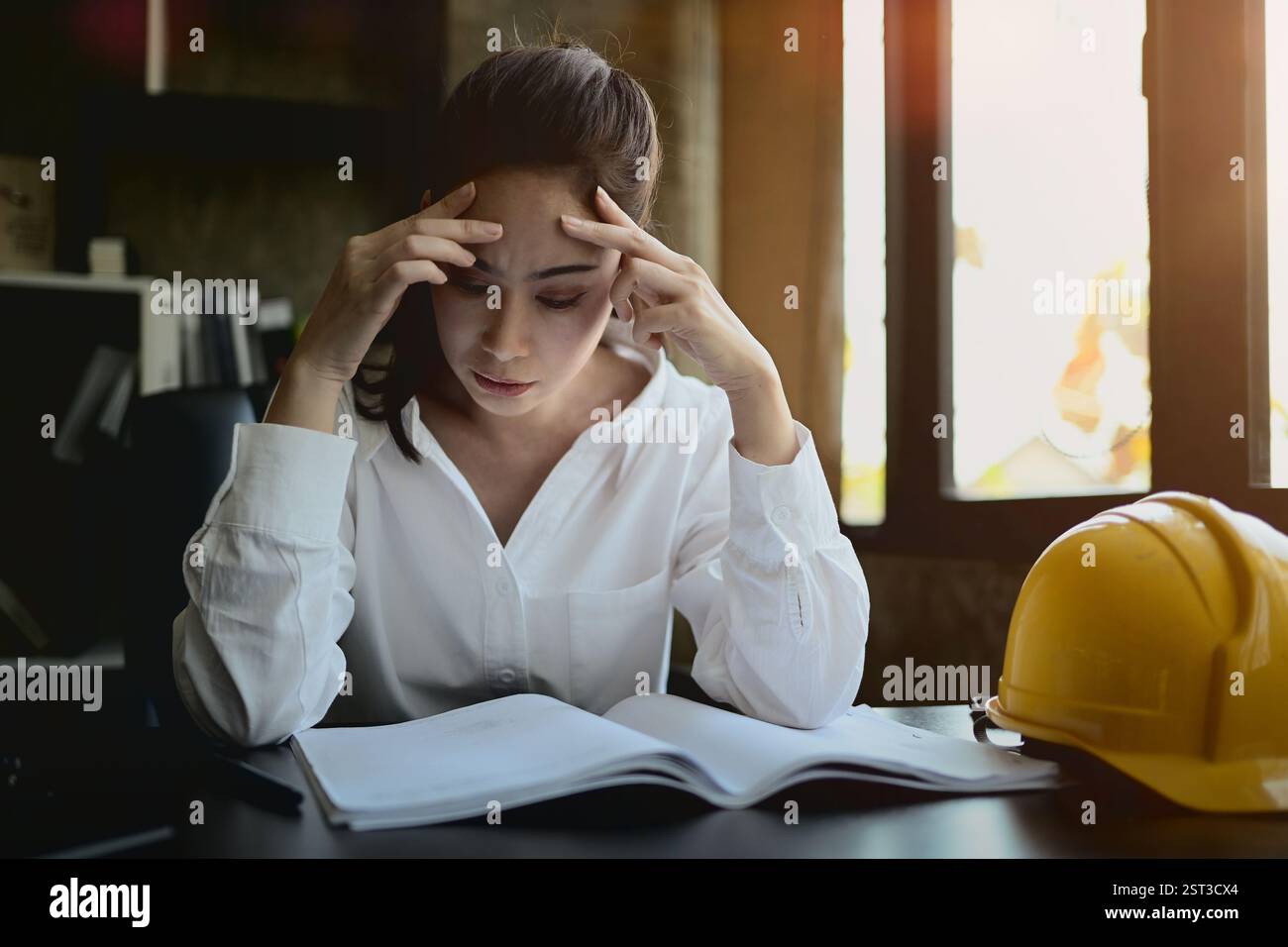 A stressed, tired Asian female architect or engineer boss sits at her ...