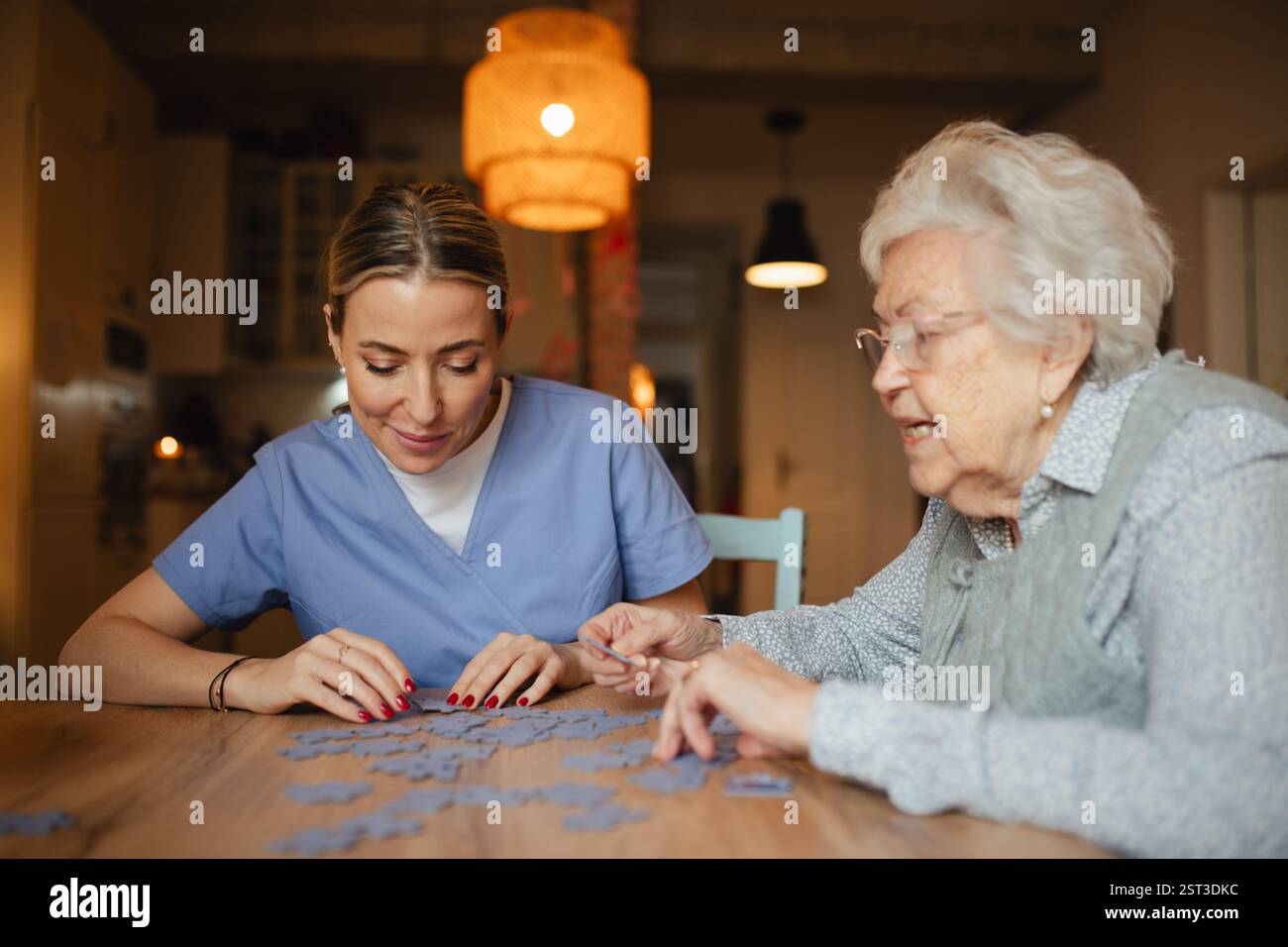 Friendly caregiver and elderly patient working on puzzle together ...