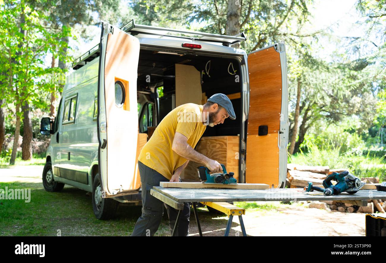 Carpenter using electric plane on wood plank, customizing camper van in ...