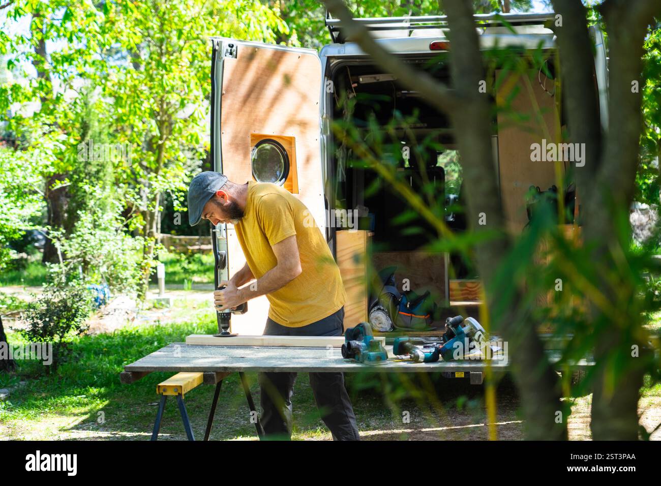 Carpenter working on wood plank near his camper van using a cordless ...