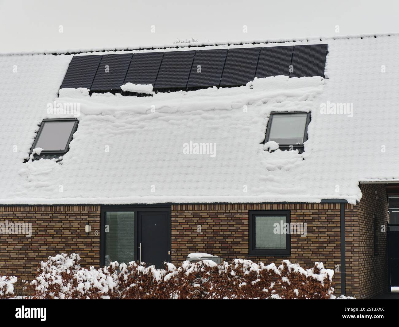 A row of modern Dutch houses with solar panels on snow-covered roofs ...
