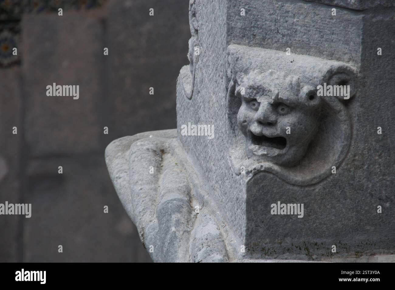 Stone grotesque face, open mouth, bulging eyes. Gargoyle-like figure ...