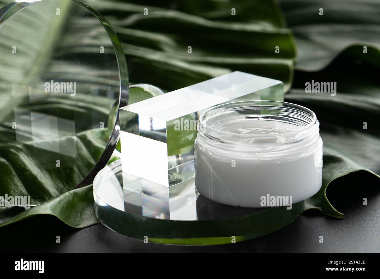 Cream container elegantly positioned on glass against a lush tropical ...