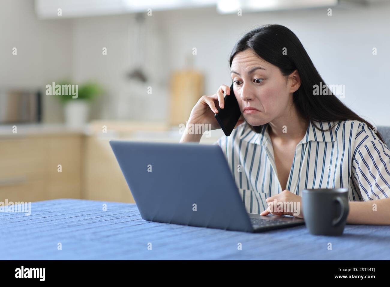 Perplexed asian woman talking on phone checking laptop in the kitchen at home Stock Photo - Alamy