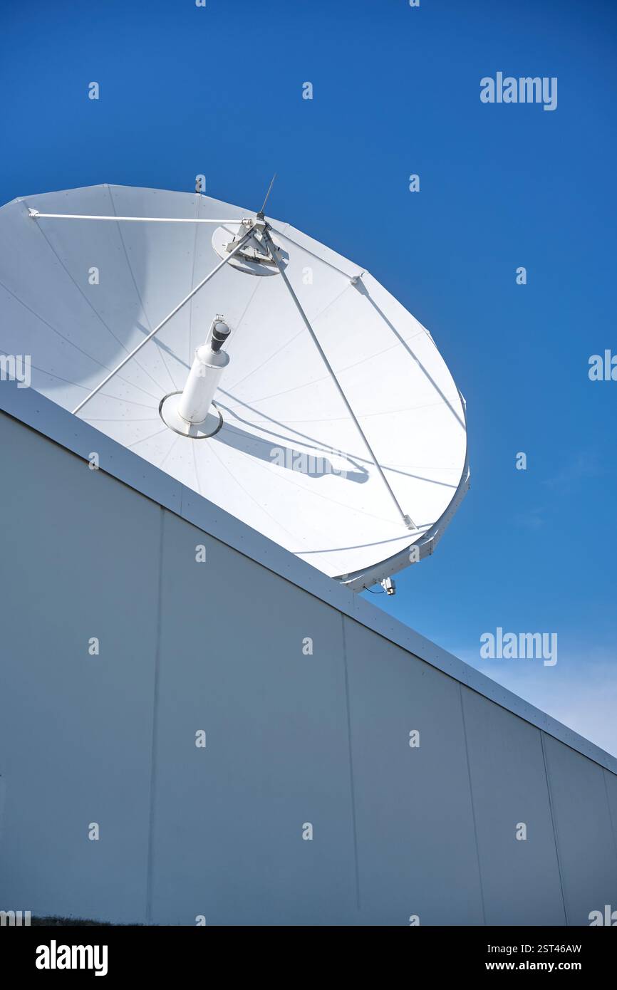 Large satellite dish communicating under blue sky on building roof ...