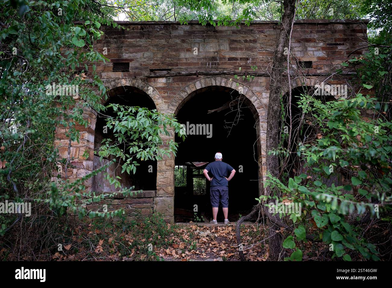 Man exploring an overgrown abandoned building with arched doorways ...