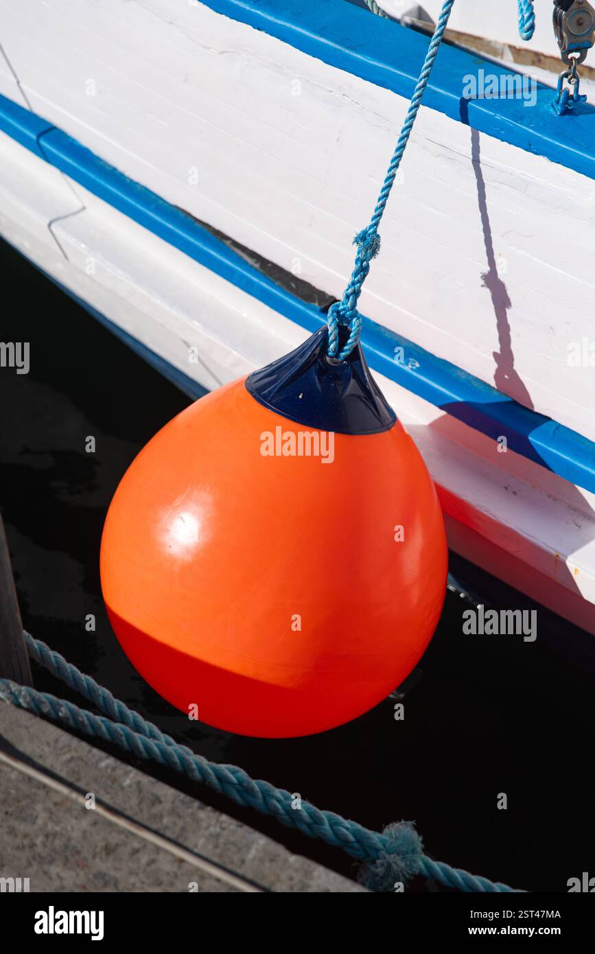Bright Orange Boat Fender Hanging between white wooden boat and dock ...