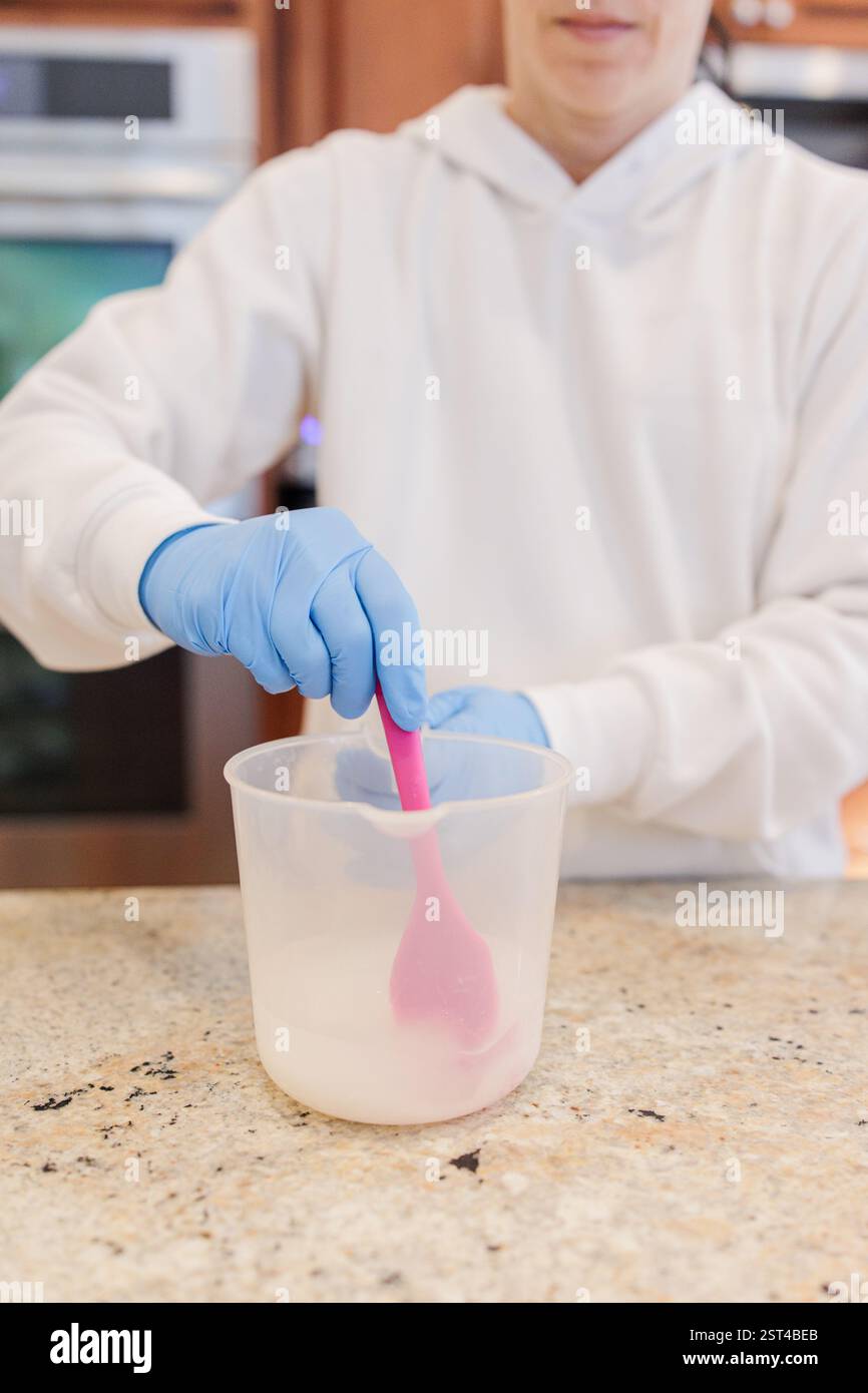 Person mixing soap ingredients in a plastic container with a spatula ...