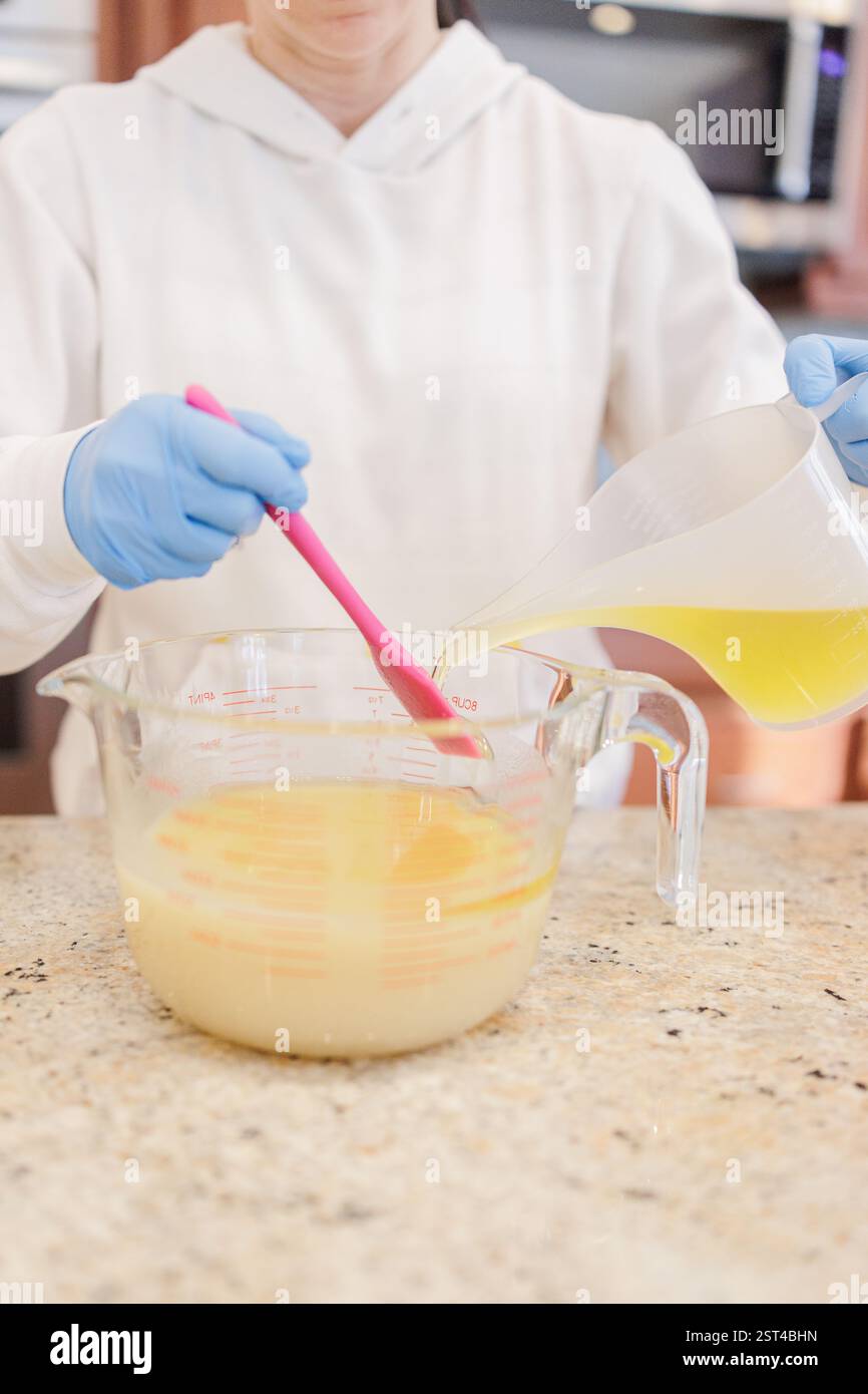 Woman pouring olive oil into lye mixture for handmade soap in Stow ...
