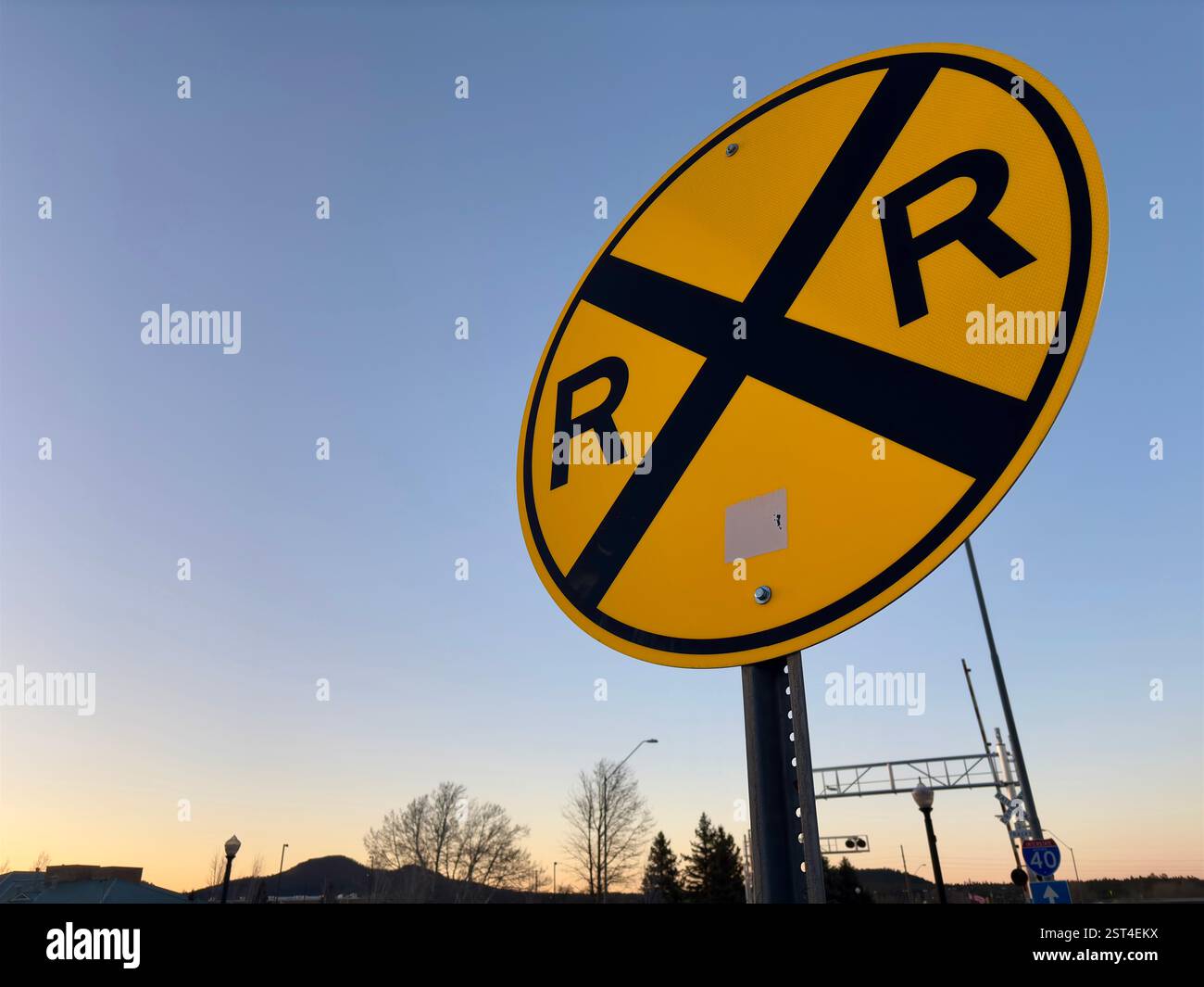 Railroad crossing sign with a sunset sky and distant traffic signals ...