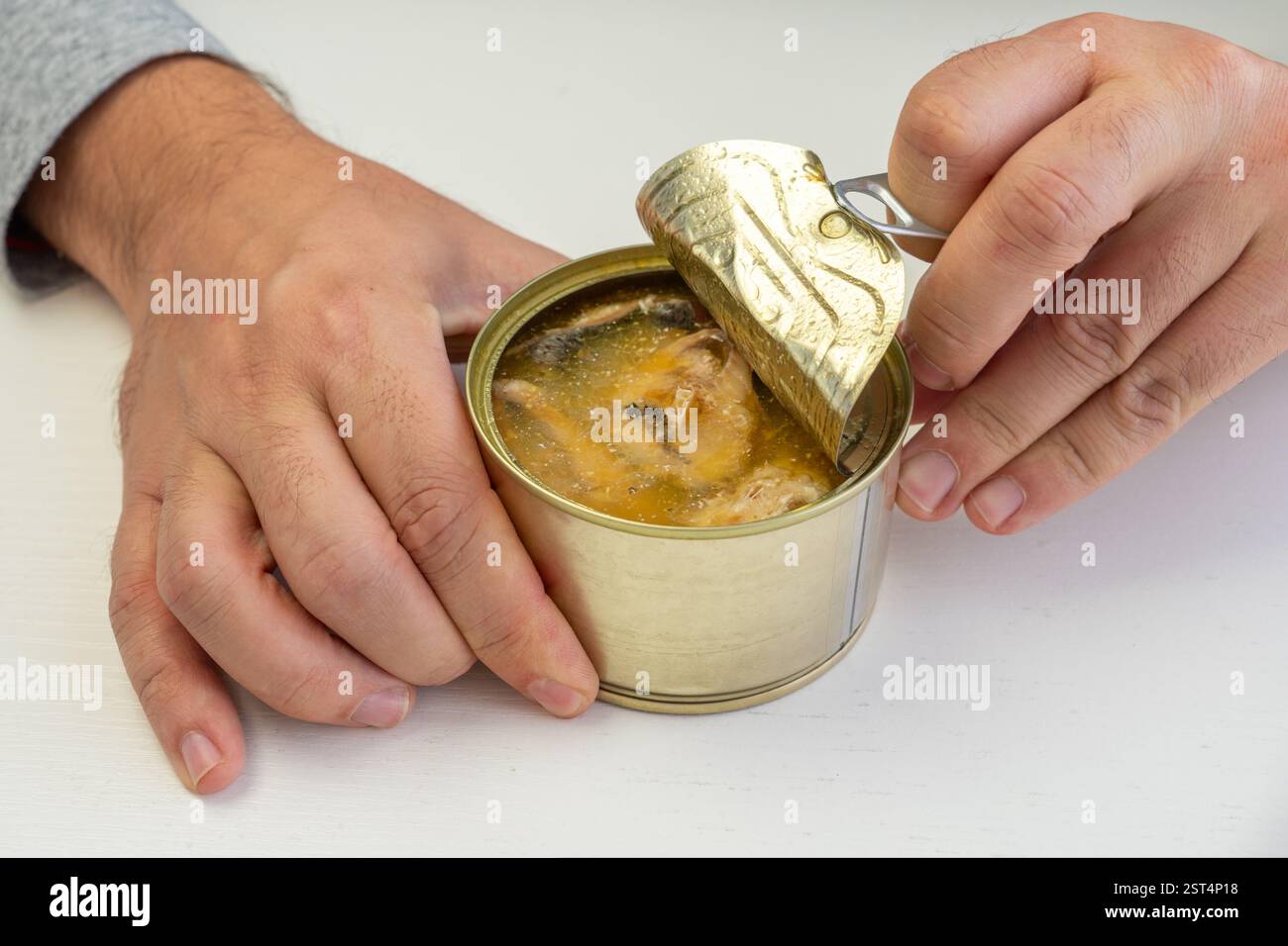 opening a tin can on a white background. Hand holds canned food on ...