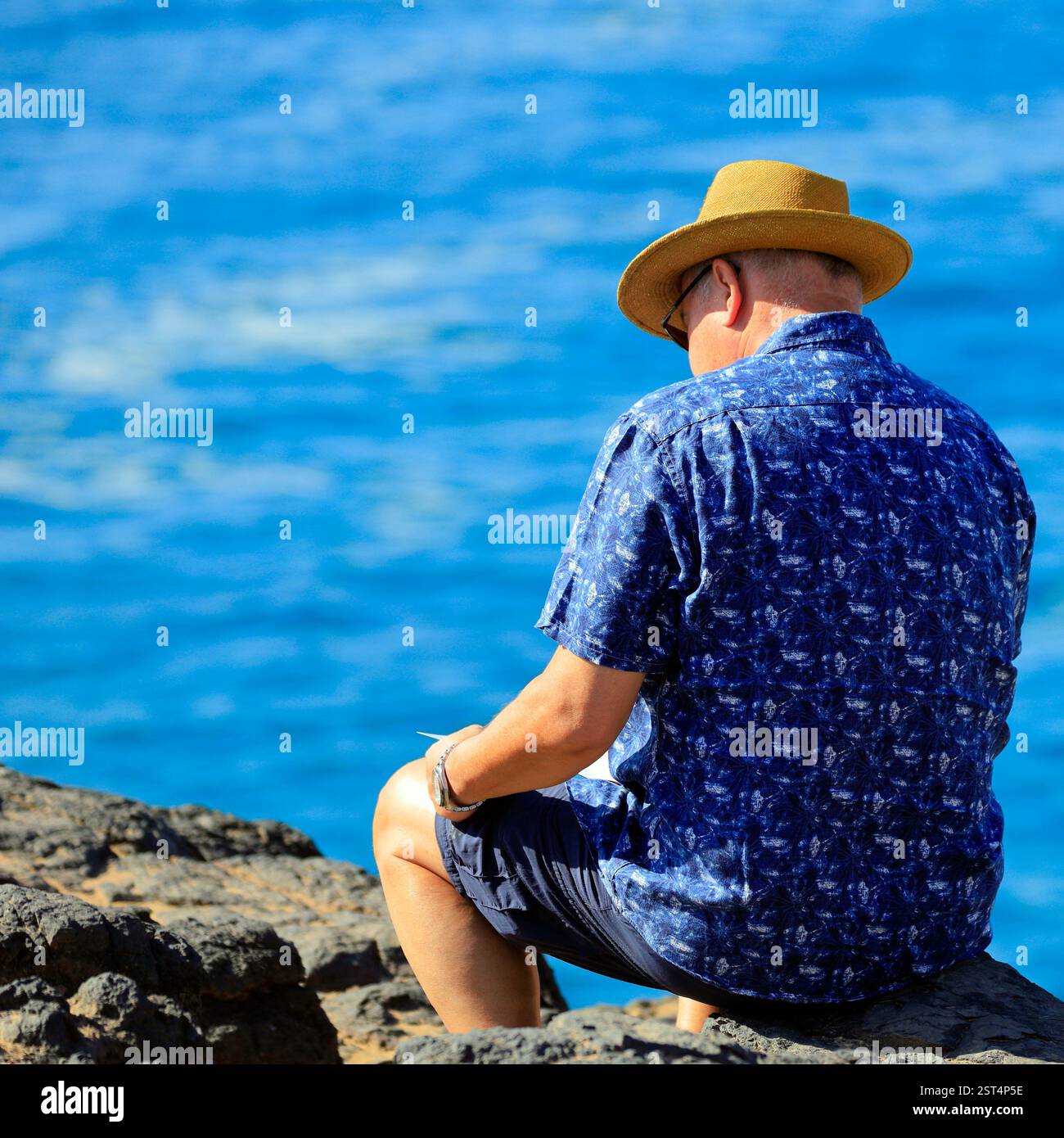 Older man in blue shirt sitting on a cliff overlooking the Atlantic ...