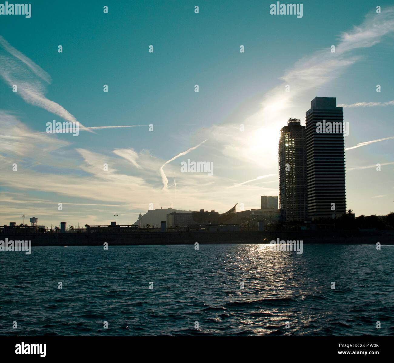 A stunning waterfront cityscape captures the sun setting behind modern ...