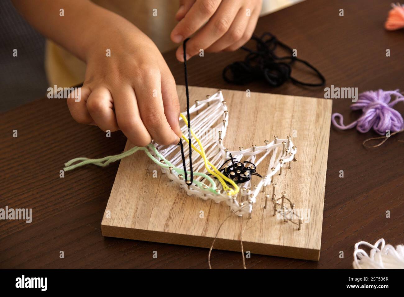 Child carefully wraps thread around tiny nails, building patience ...