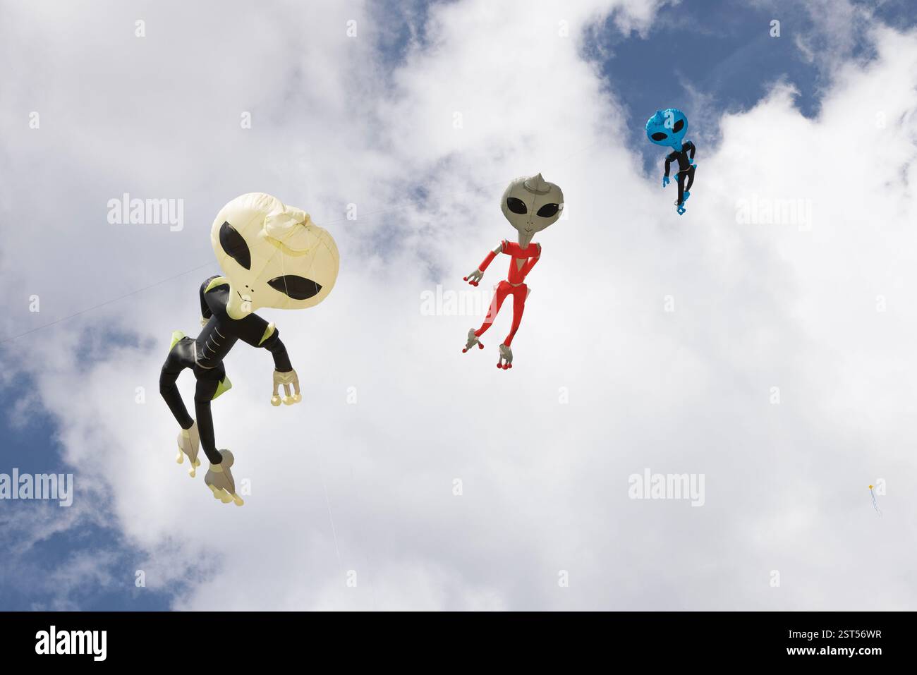 Alien-shaped balloons floating against a blue sky with clouds, creating ...