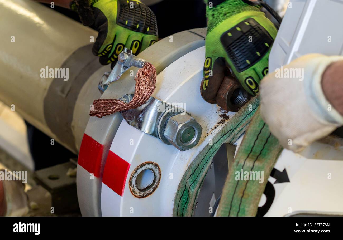 Workers dismantling a flanged pipeline connection using lifting straps ...
