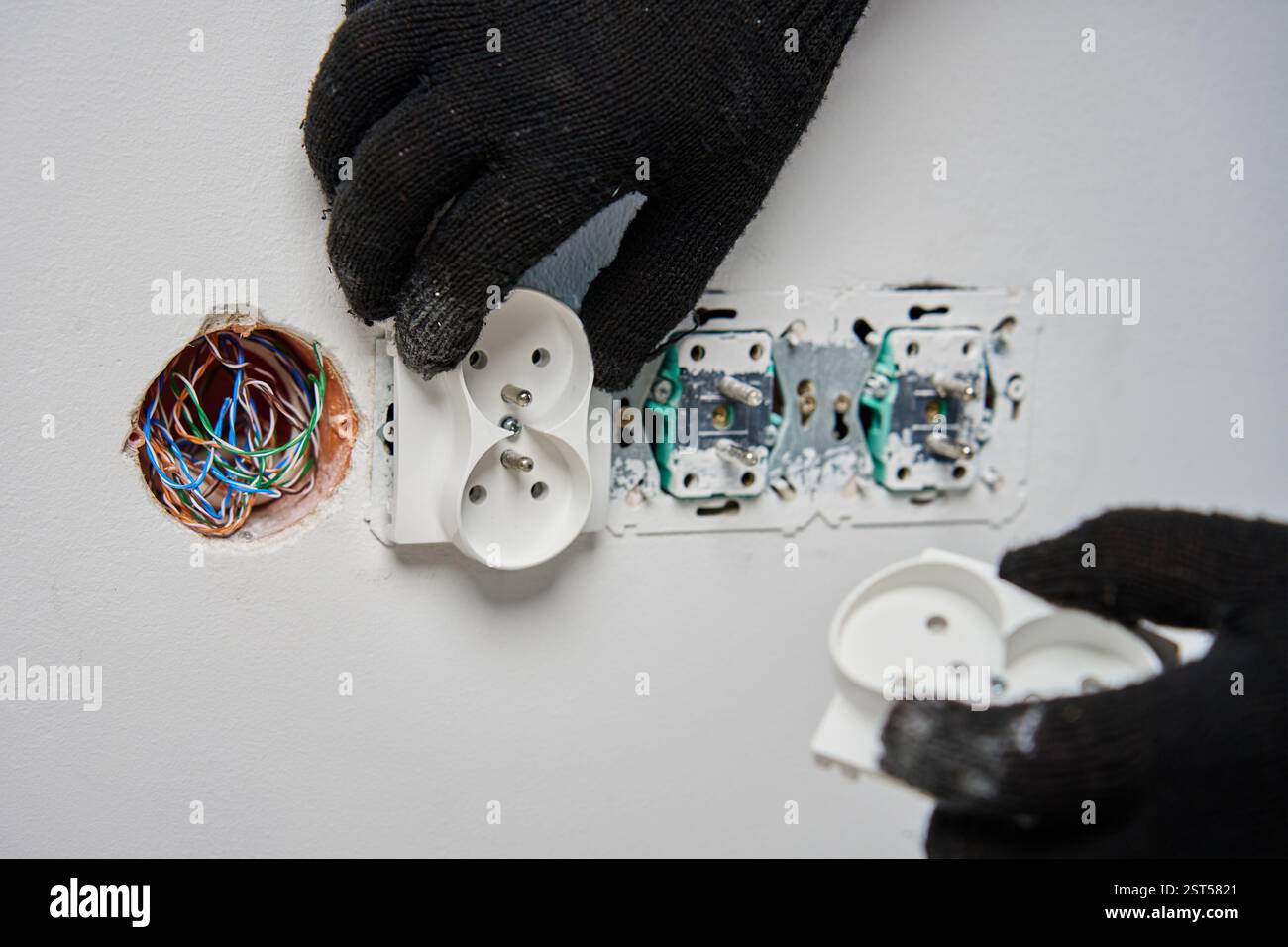 Close-up of an electrician wearing black gloves installing power socket ...