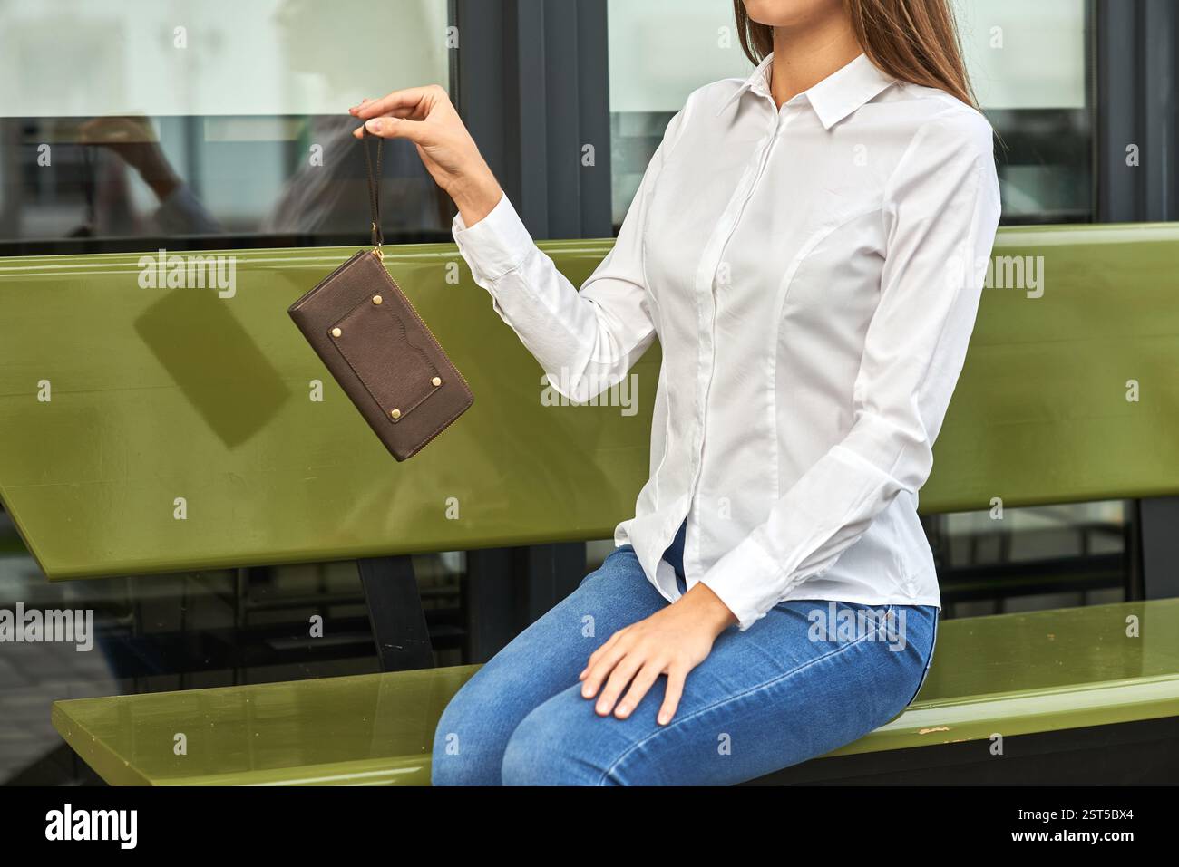 Woman wearing casual outfit sitting on park bench holding a brown ...