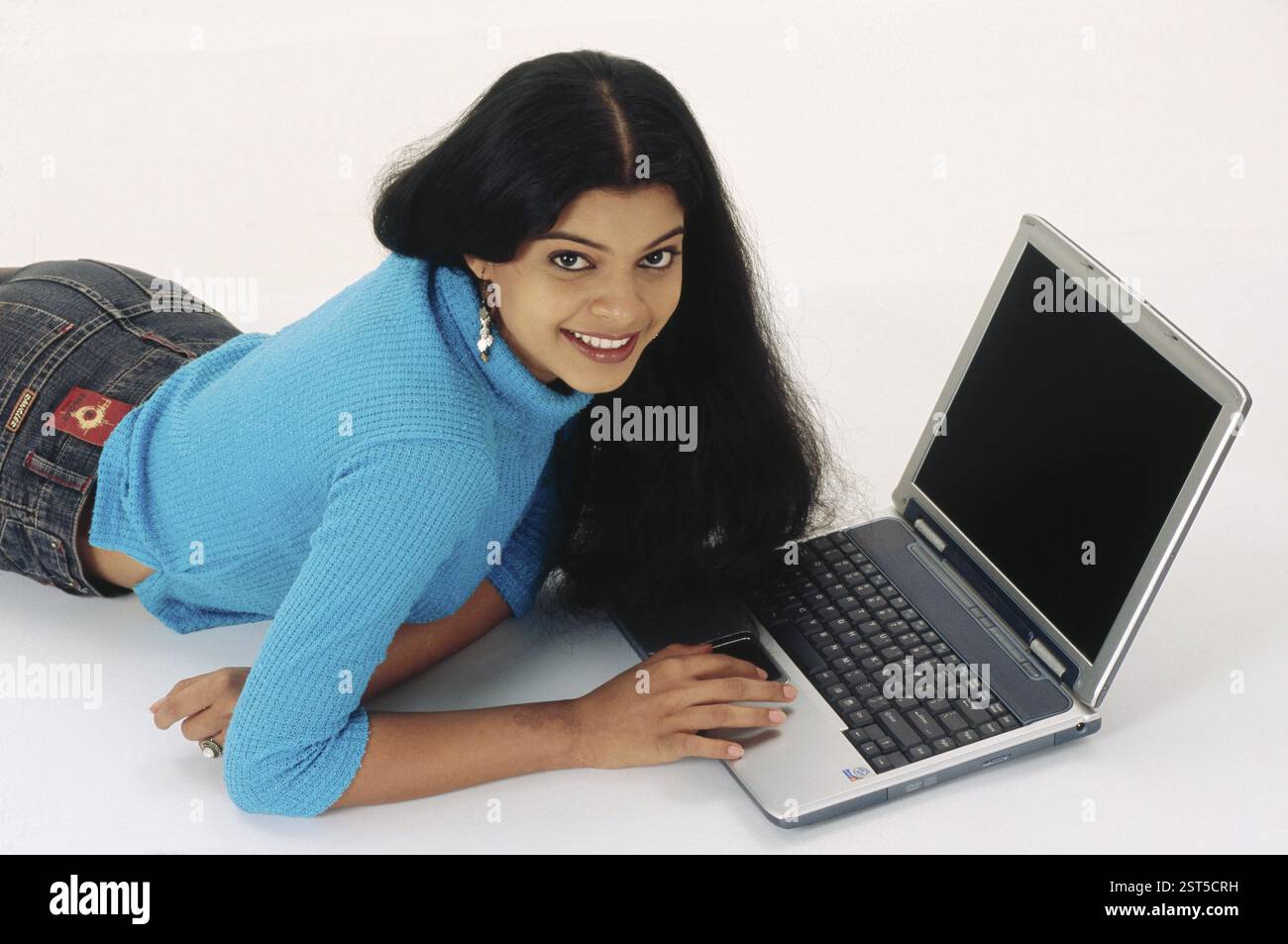 South Asian Indian executive lady lying down on floor operating laptop ...