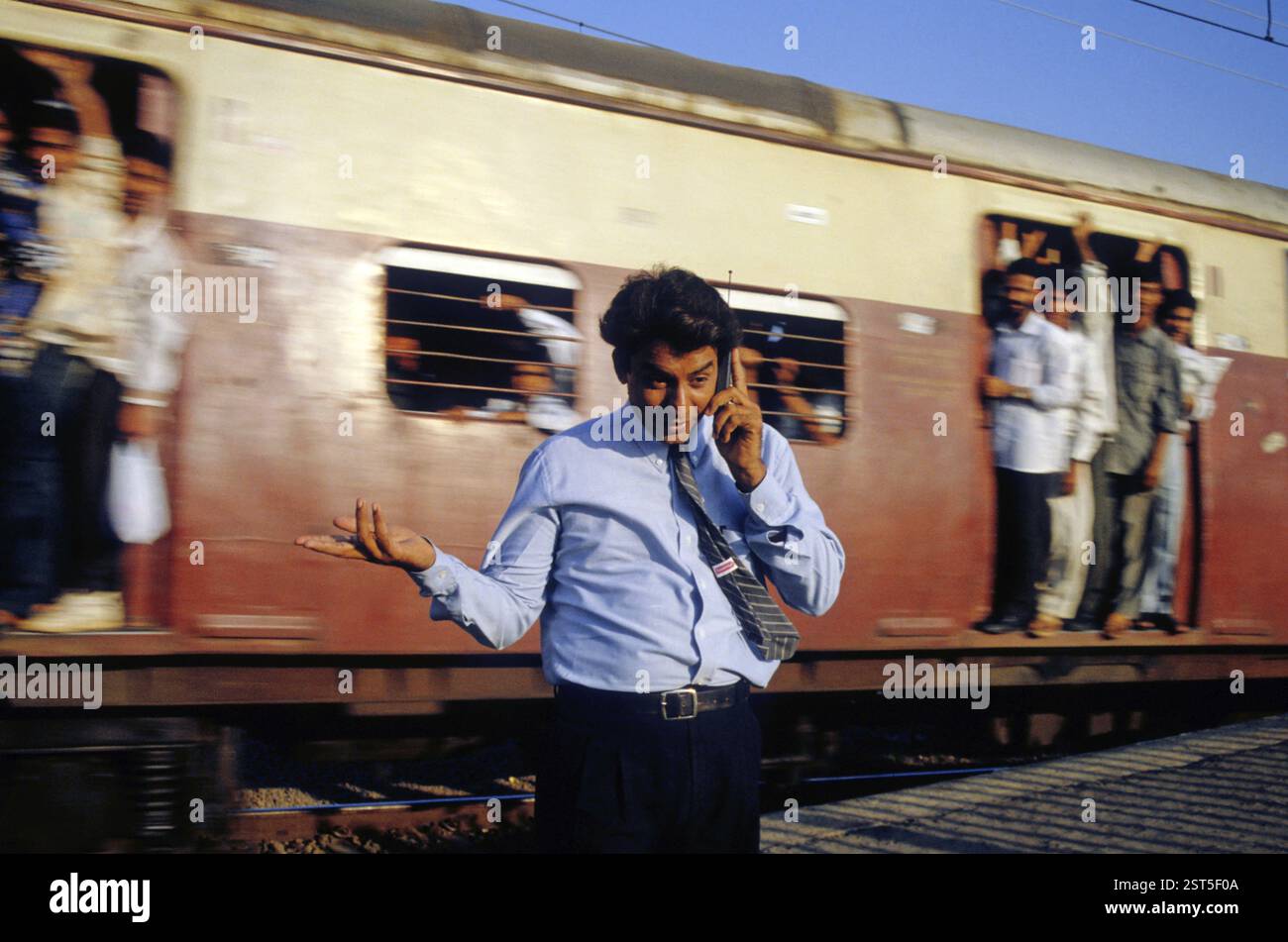 Man talking on mobile phone in front of suburban train in Bombay Mumbai ...
