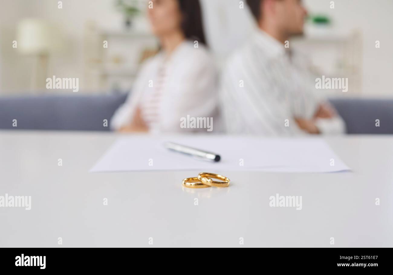 Wedding rings with marriage contract on table and unhappy couple ...