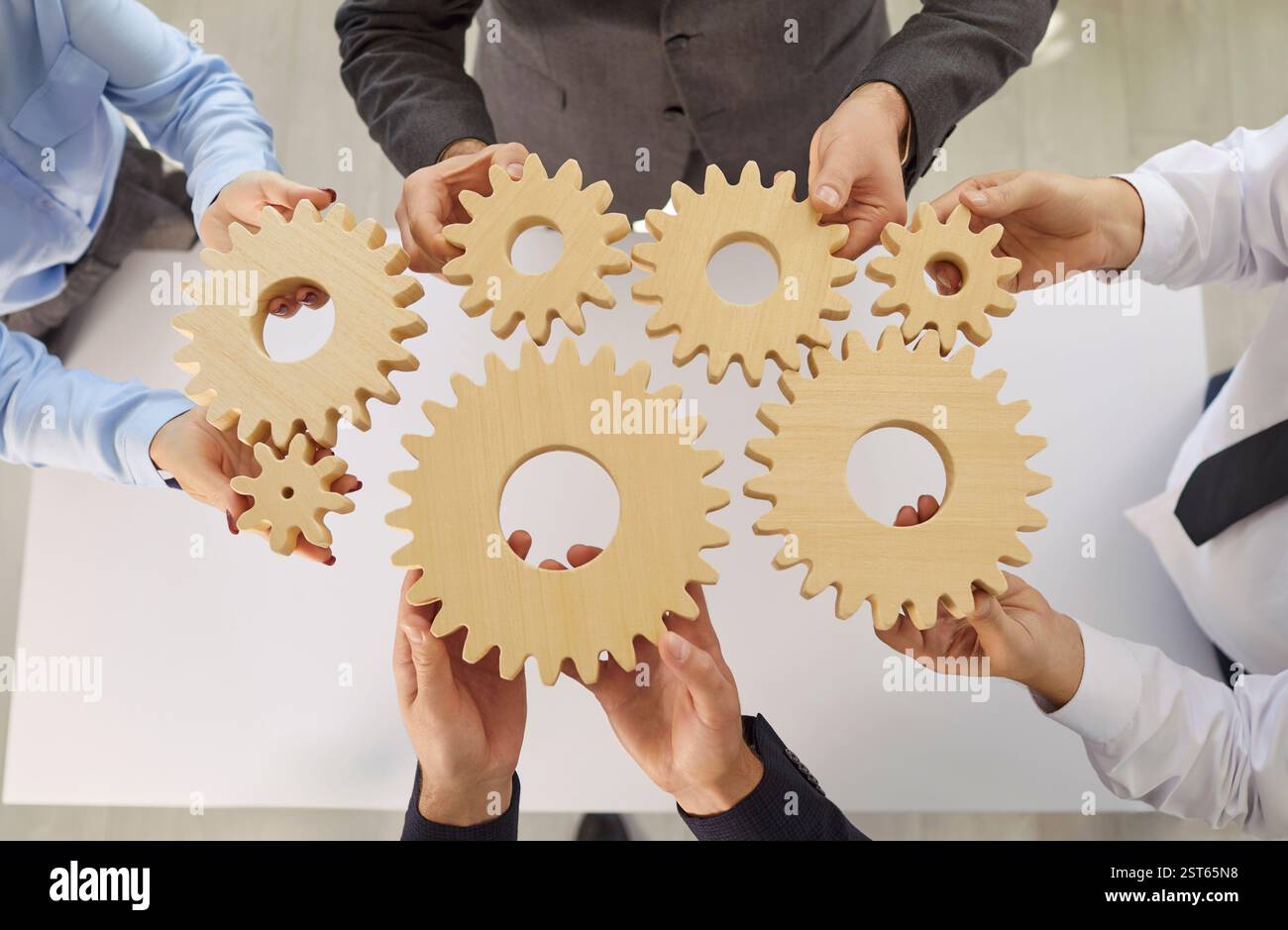 Business team of four stacking wooden gear wheels together, symbolizing ...