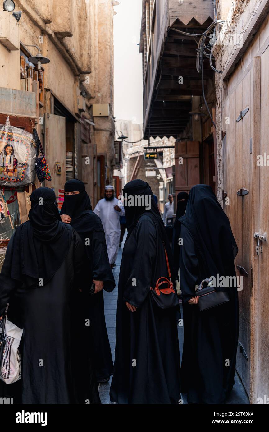 Women in black abayas walk through a narrow alley in a Middle Eastern ...