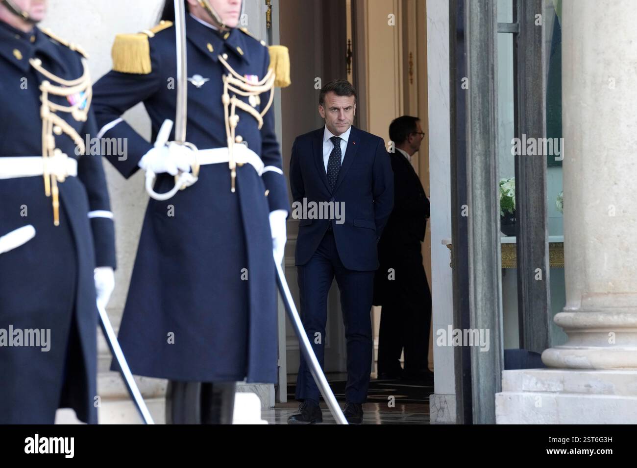 French President Emmanuel Macron walks out of a doorway as he waits for ...