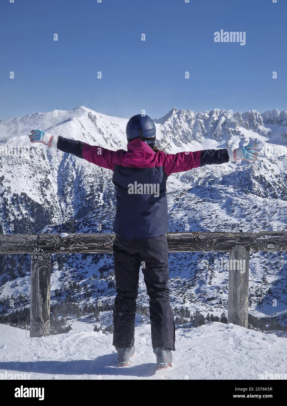Rear view woman skier on the mountain top standing with arms wide open ...