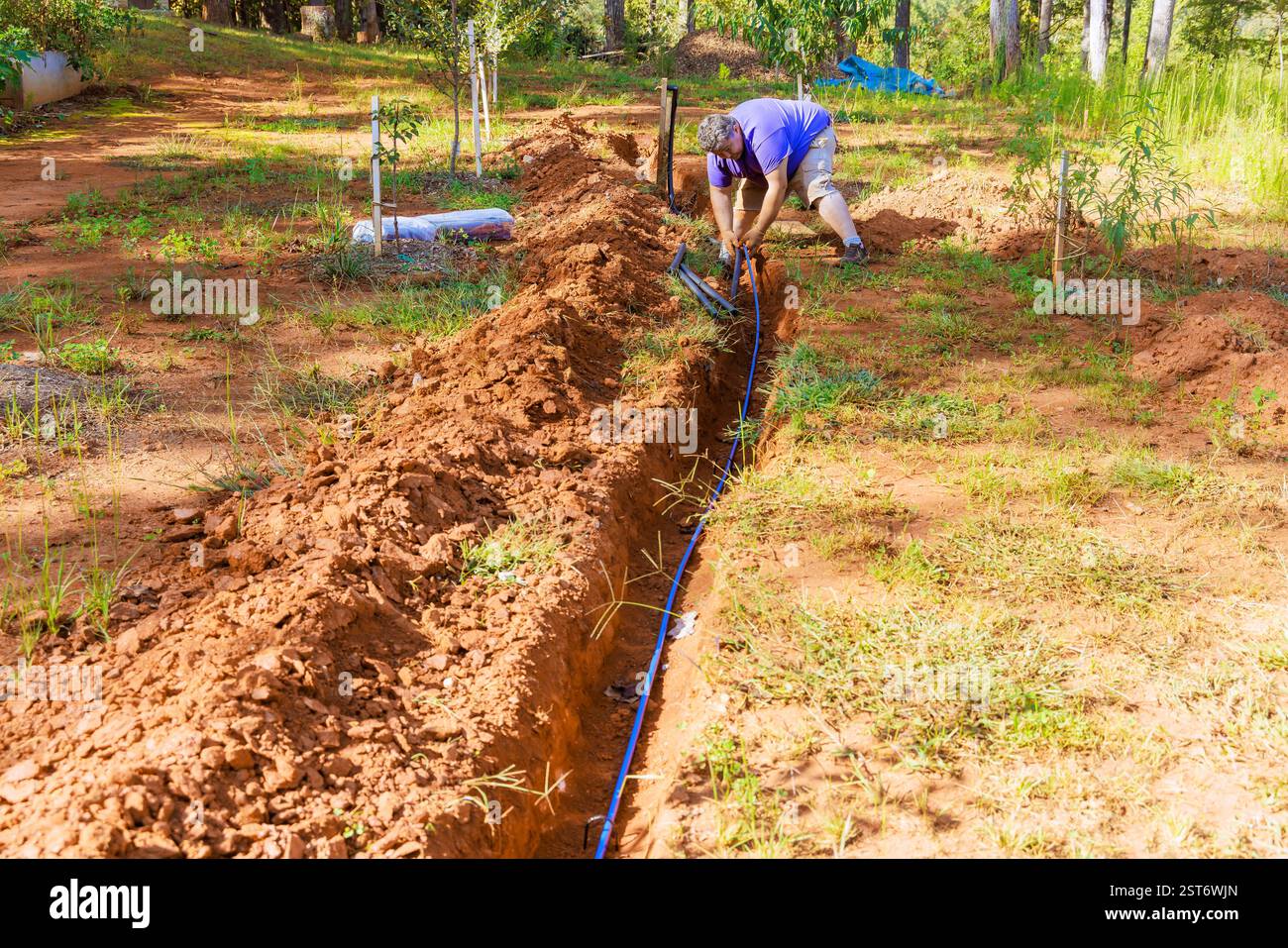 Plumber works diligently to dig trench install an PVC water pipe ...