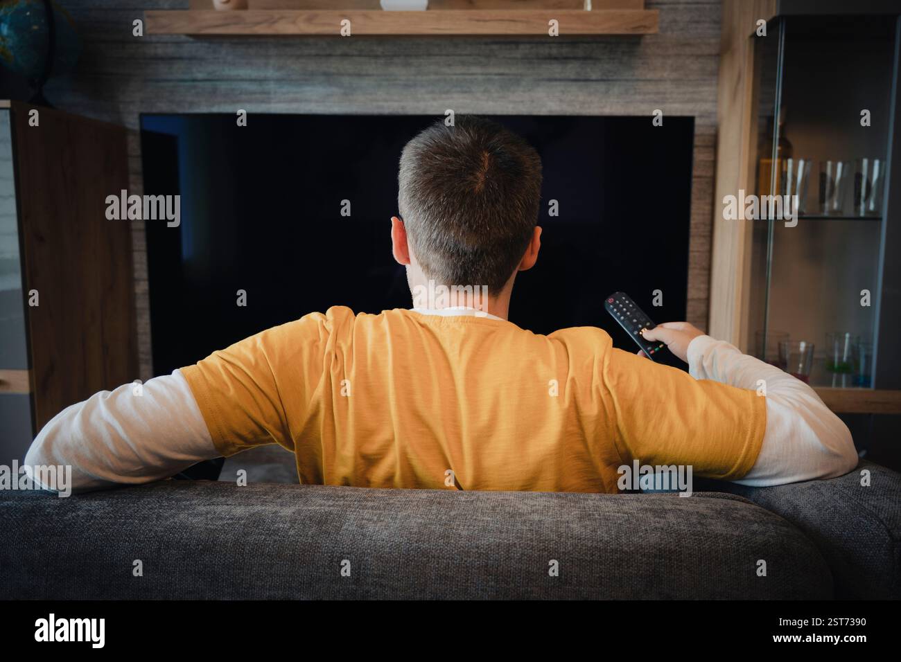 Man watching television, turning on plasma flatscreen TV-set, pointing remote control at empty ...