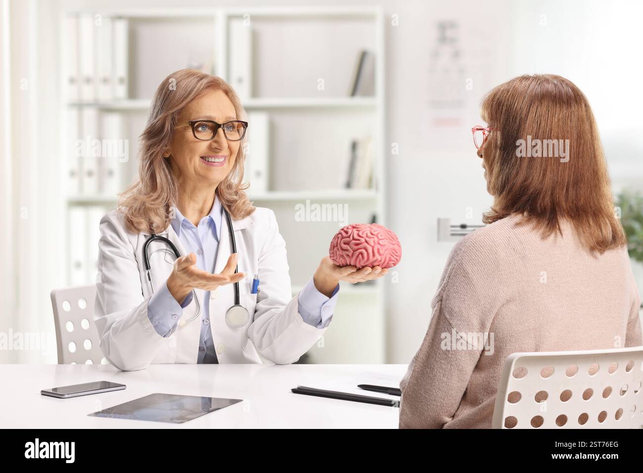 Psychiatrist sitting with a patient and holding a brain model at the ...