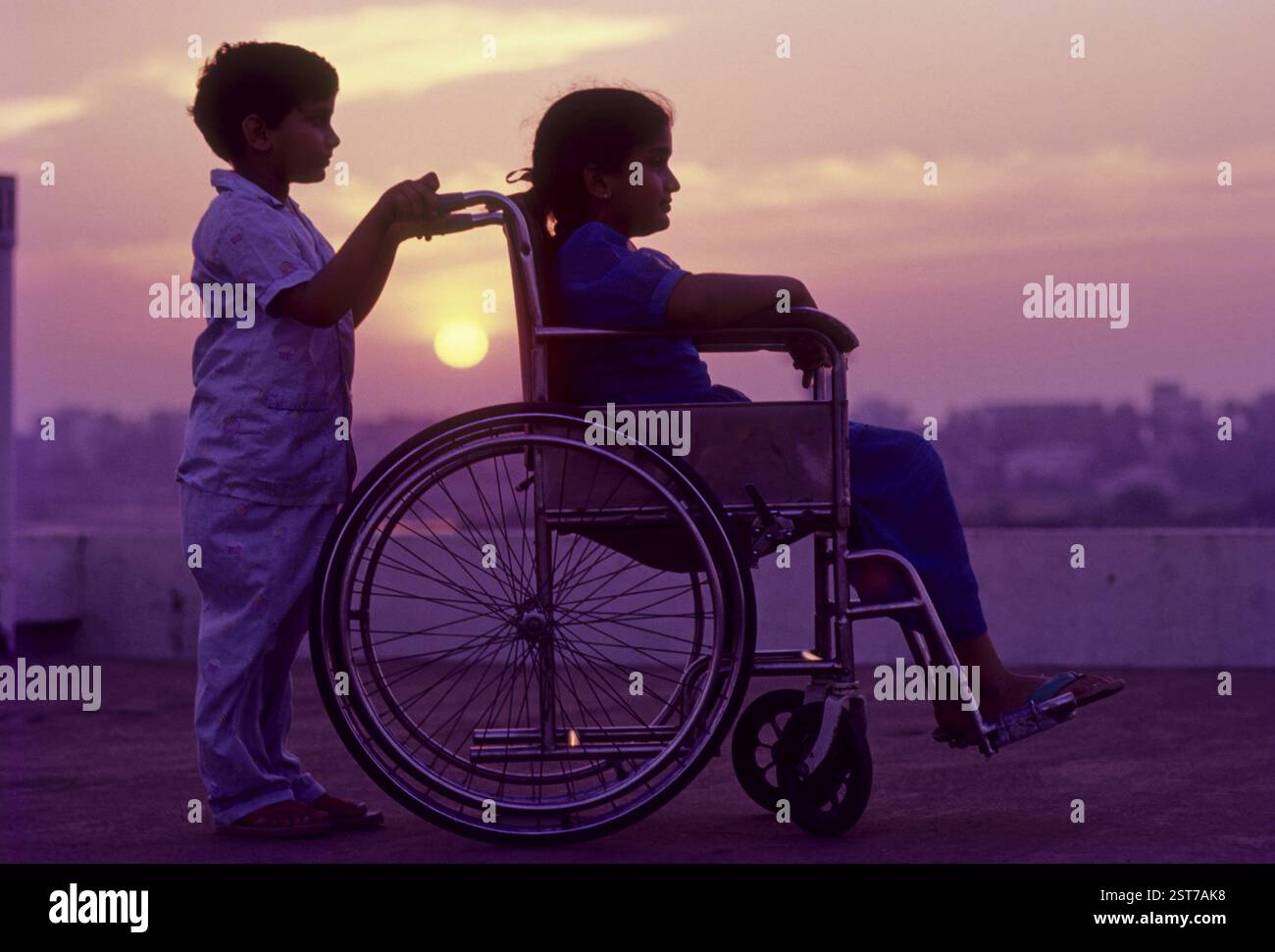 Girl sitting on Wheelchair and boy standing behind Stock Photo - Alamy