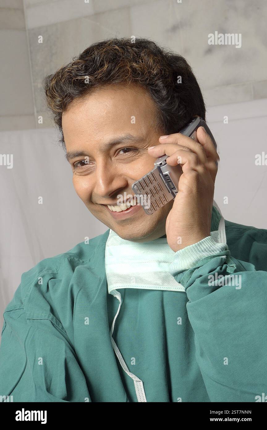 Young Indian Doctor surgeon smiling, talking on mobile phone, in green ...