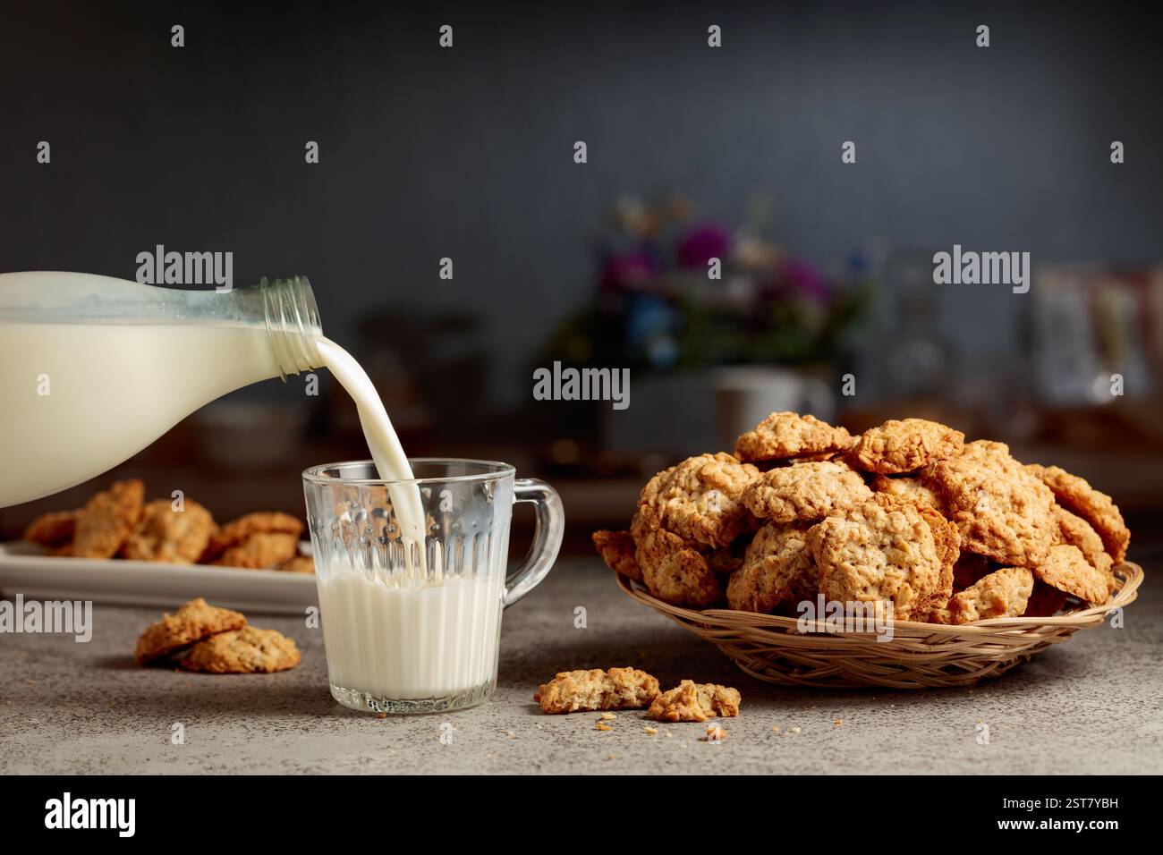 Oatmeal cookies and milk on a kitchen table. Milk is poured from a ...