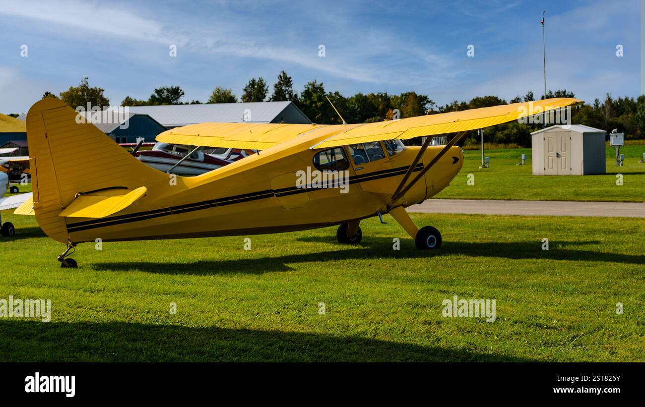 Yellow private airplane next to hangars and a runway in the summer ...