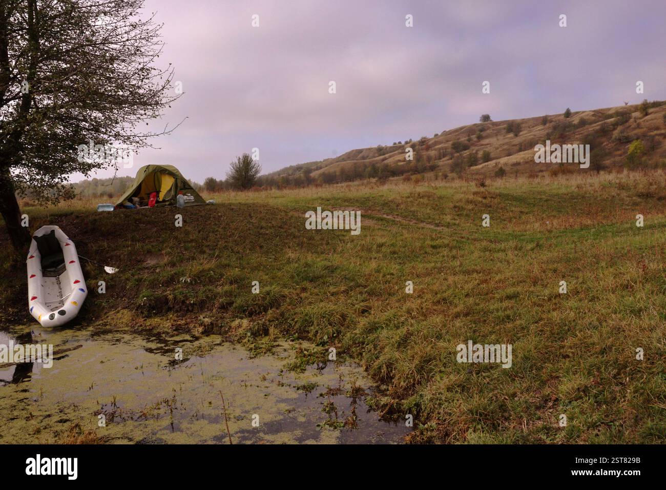 A lone canoeist camping on the river bank under a colorful relief hill ...