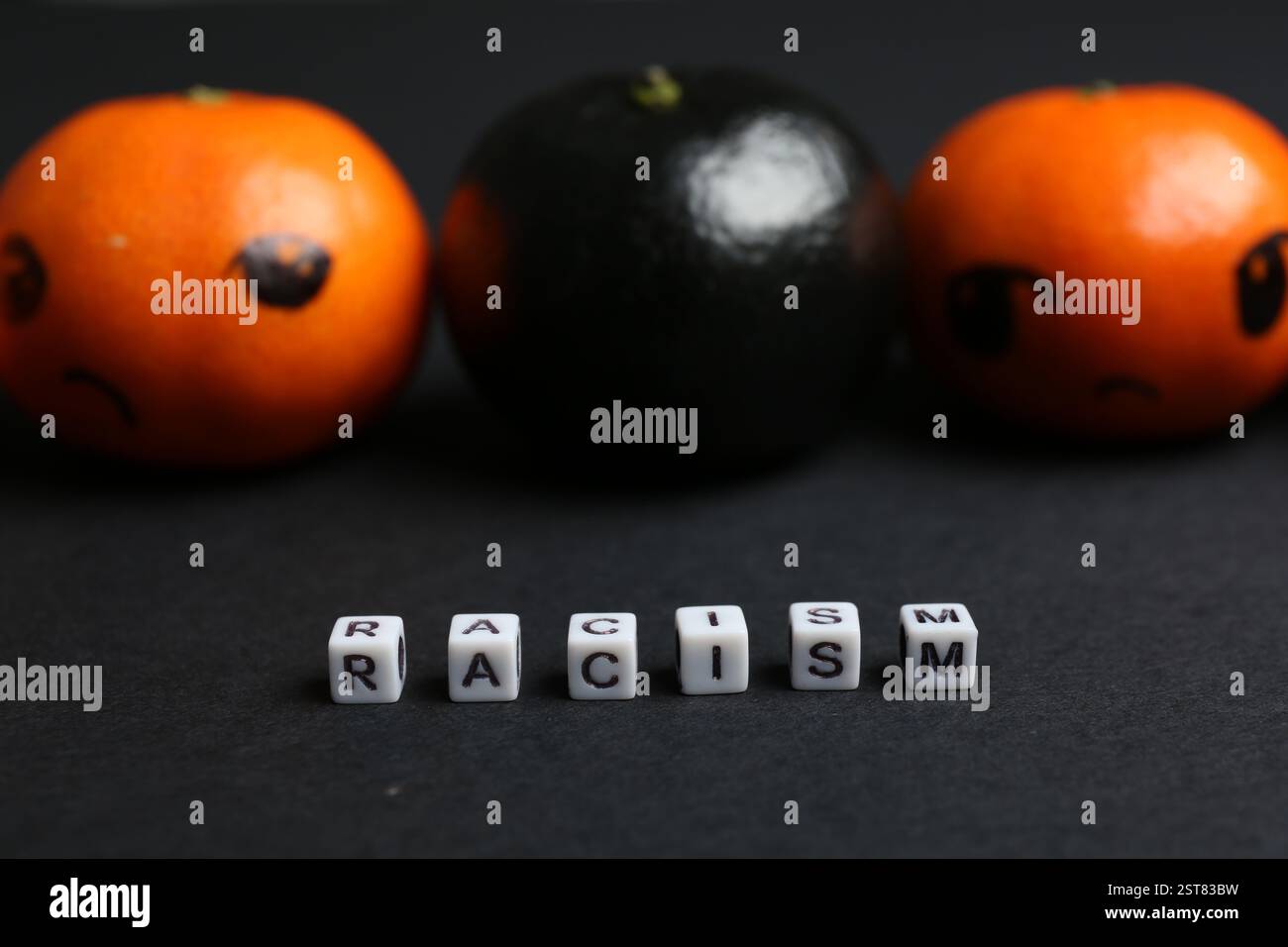 One black tangerine among orange ones and word Racism made with beads ...