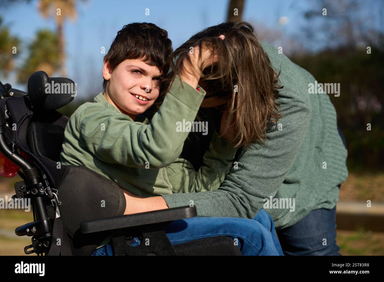 Boy with cerebral palsy playing with his mother's hair in a wheelchair ...